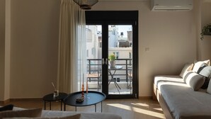 Uma sala de estar moderna com um sofá, uma mesa pequena e uma varanda com vista para a cidade.