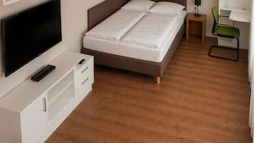 Quarto de hotel com cama, televisão, escrivaninha e cadeira.