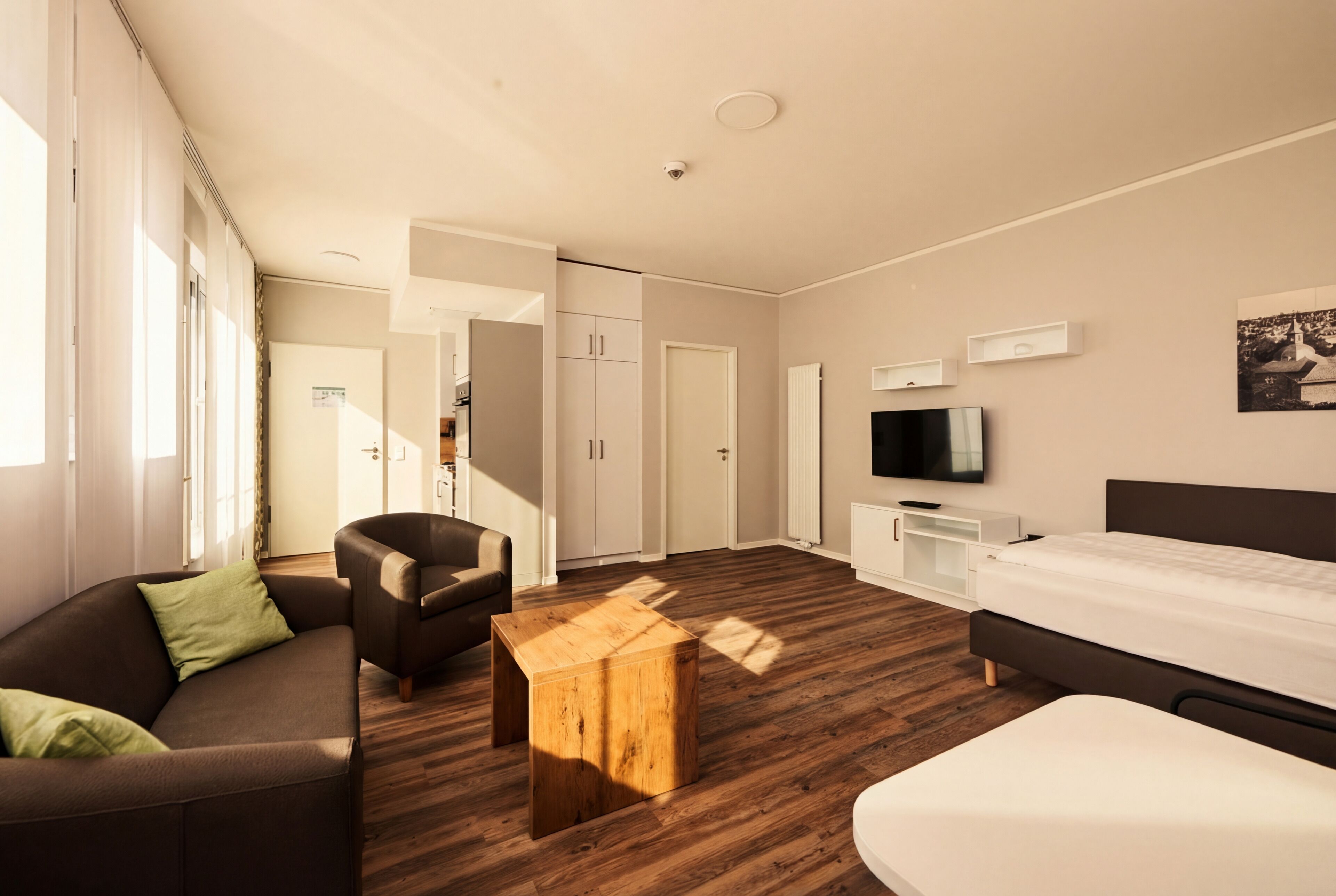 Quarto de hotel moderno com cama, sofá, mesa de centro de madeira, televisão e guarda-roupa.