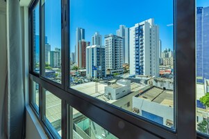 Vista da janela com vista para um horizonte urbano, prédios altos e céu azul límpido.