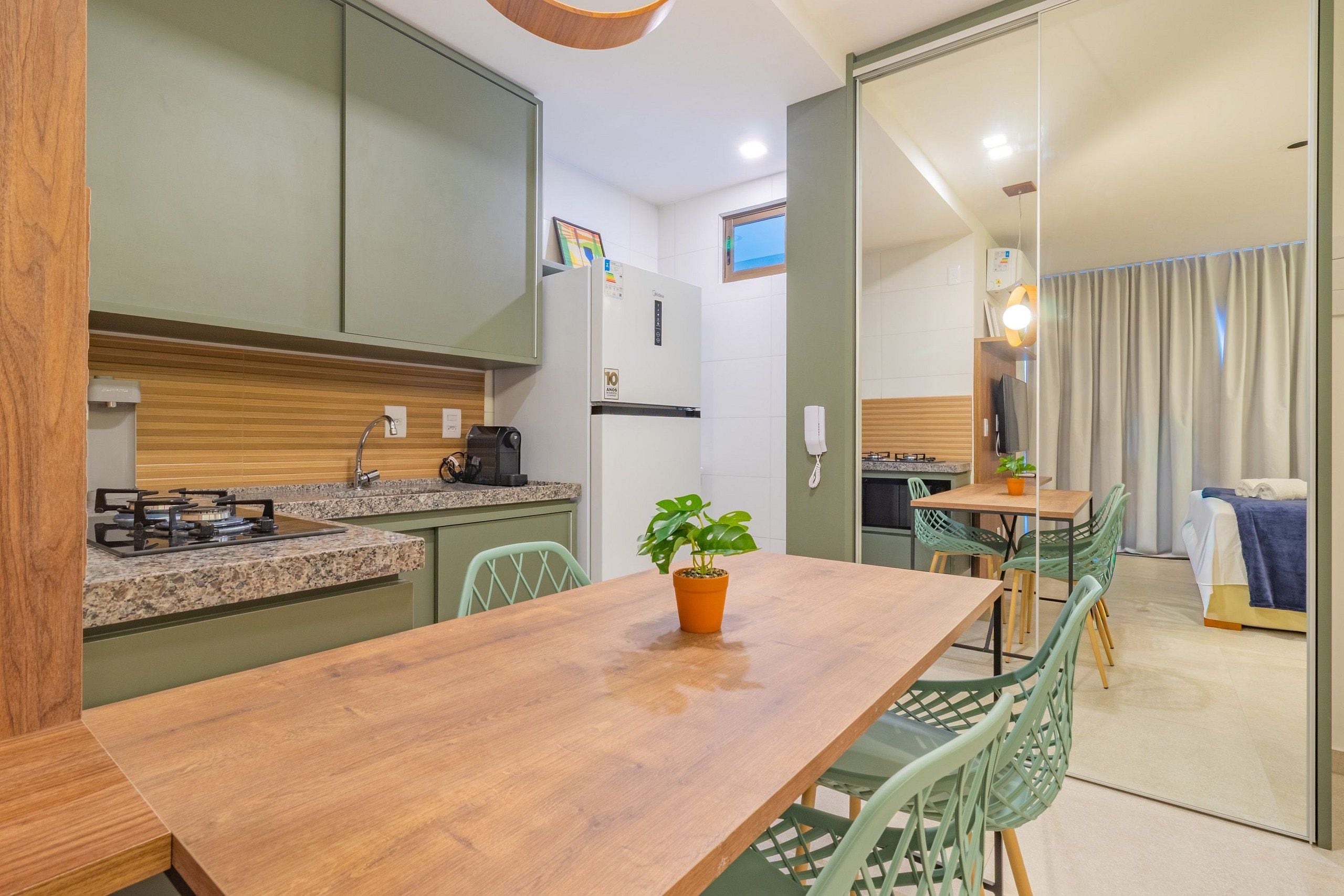 Uma cozinha compacta com uma mesa e cadeiras de madeira, geladeira e um vaso de planta.