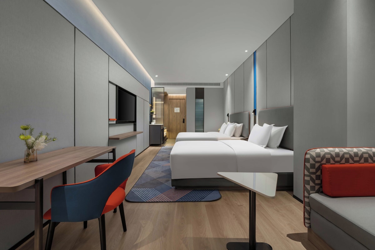 Quarto de hotel moderno com cama, sofá, escrivaninha e televisão.