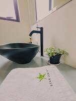 Casa de banho com lavatório preto, torneira preta, toalha branca e uma pequena planta em vaso.