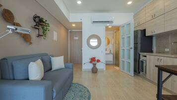 Uma sala de estar moderna com um sofá, uma mesa de centro e um vaso com flores. Há uma área de cozinha com armários e uma geladeira.