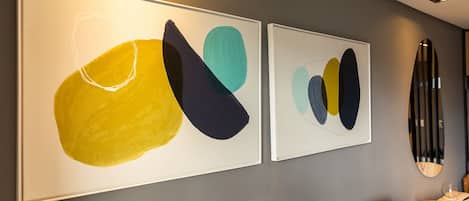 Duas pinturas abstratas na parede, um sofá cinzento e uma mesa de apoio de madeira com um copo.