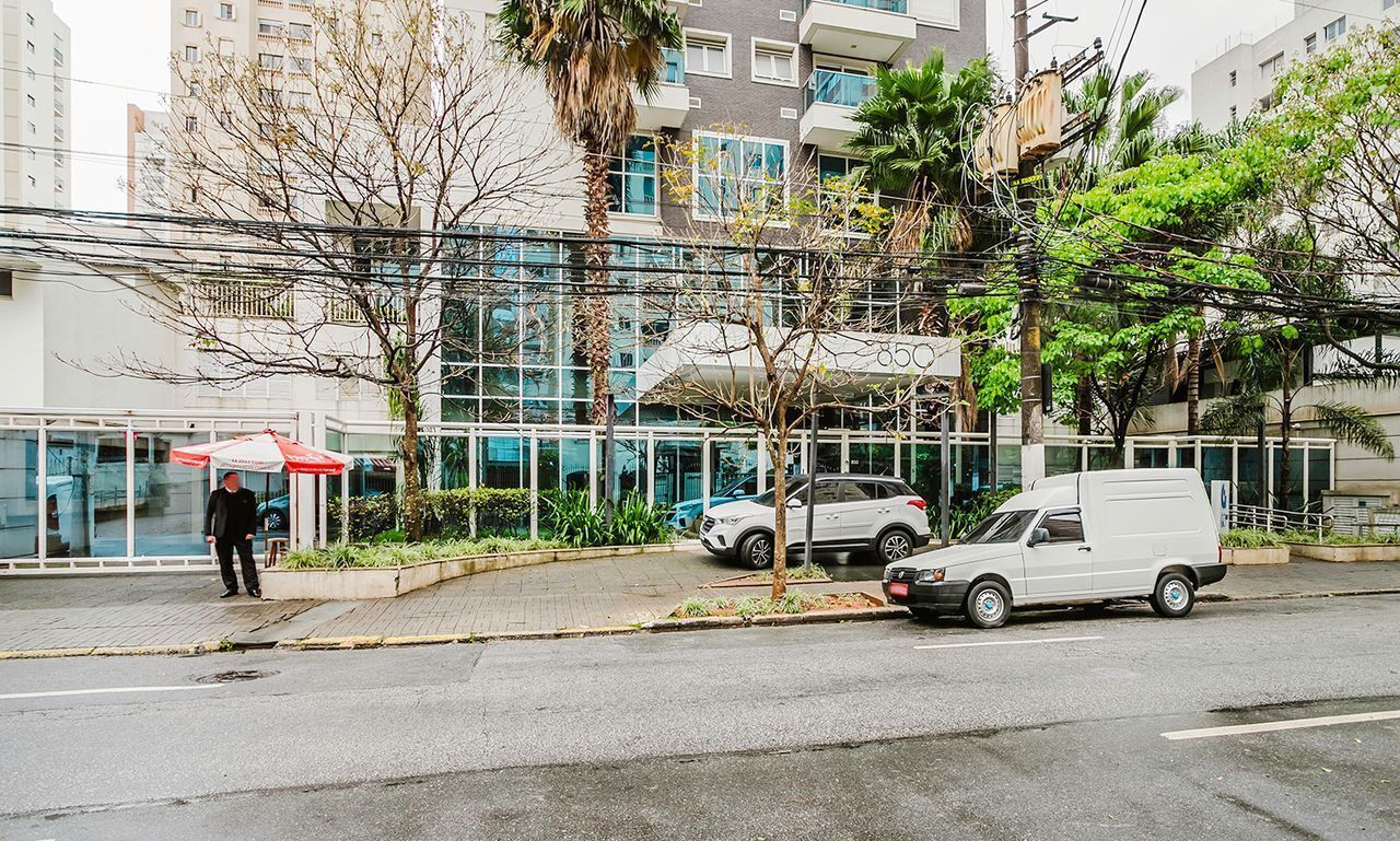Um edifício moderno com fachada de vidro, uma carrinha branca estacionada em frente e uma pessoa na passeata.