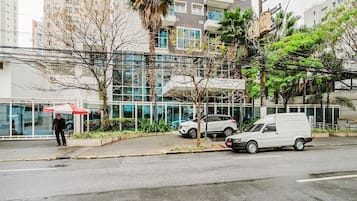 Um edifício moderno com fachada de vidro, uma carrinha branca estacionada em frente e uma pessoa na passeata.