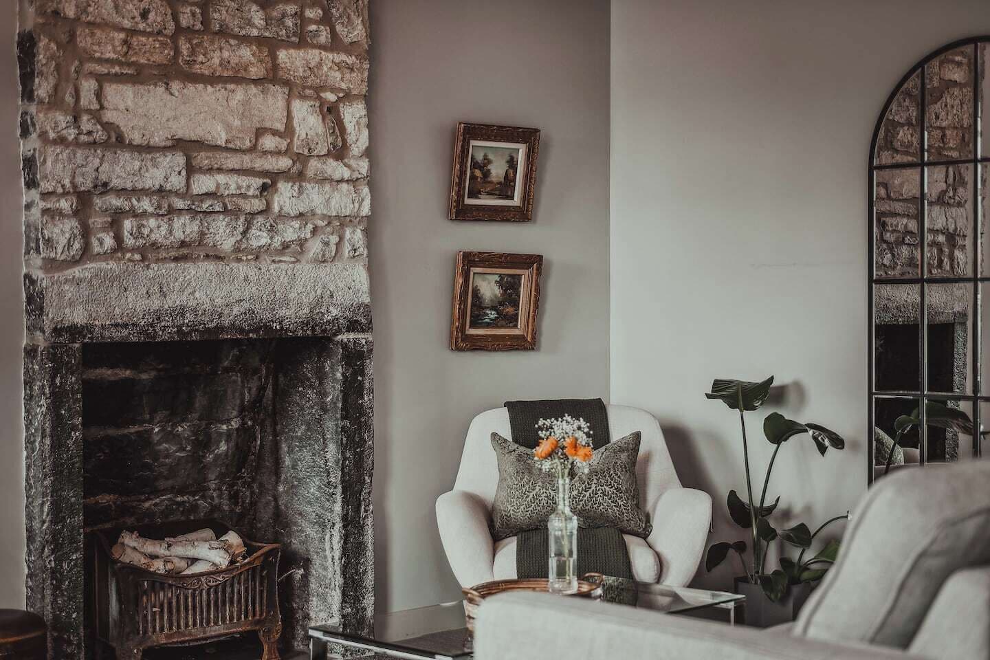 Uma sala de estar aconchegante com lareira de pedra, uma poltrona branca e duas fotos emolduradas na parede.