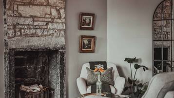 Uma sala de estar aconchegante com lareira de pedra, uma poltrona branca e duas fotos emolduradas na parede.