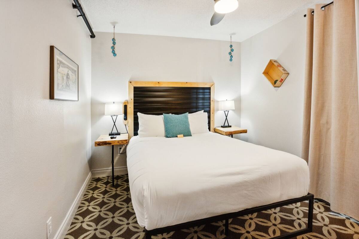 Quarto de hotel bem arrumado com uma cama grande, duas mesas de cabeceira, uma cabeceira e um tapete estampado.