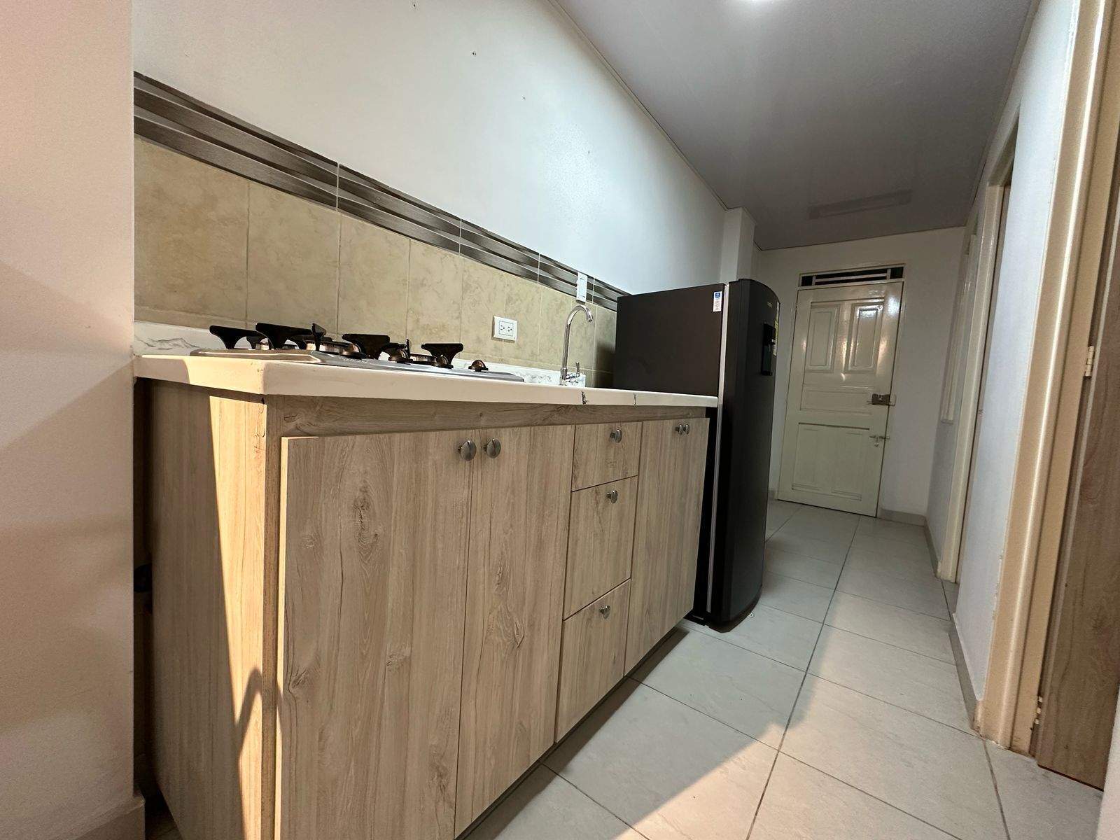 Uma cozinha com armário de madeira, geladeira preta e painel de azulejos.