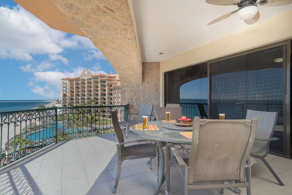Uma varanda com mesa, cadeiras e vista para o oceano e edifícios do hotel.