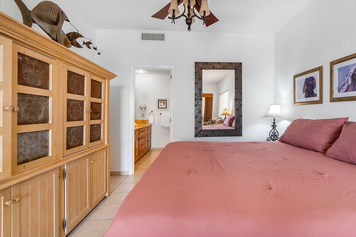 Quarto com uma cama grande, armários de madeira, um espelho e duas molduras na parede.