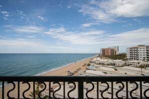 Vista da praia com céu claro, areal e edifícios ao fundo.