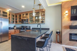 Cozinha moderna com ilha central, banquetas, micro-ondas e armários de madeira.