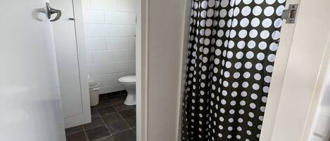 Casa de banho pequena com cortina de chuveiro estampado com bolinhas, porta branca e sanita visível ao fundo.