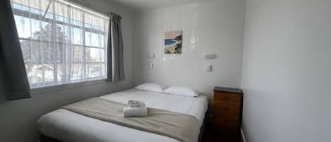 Quarto com cama, mesa de cabeceira, janela com cortinas e quadro na parede.