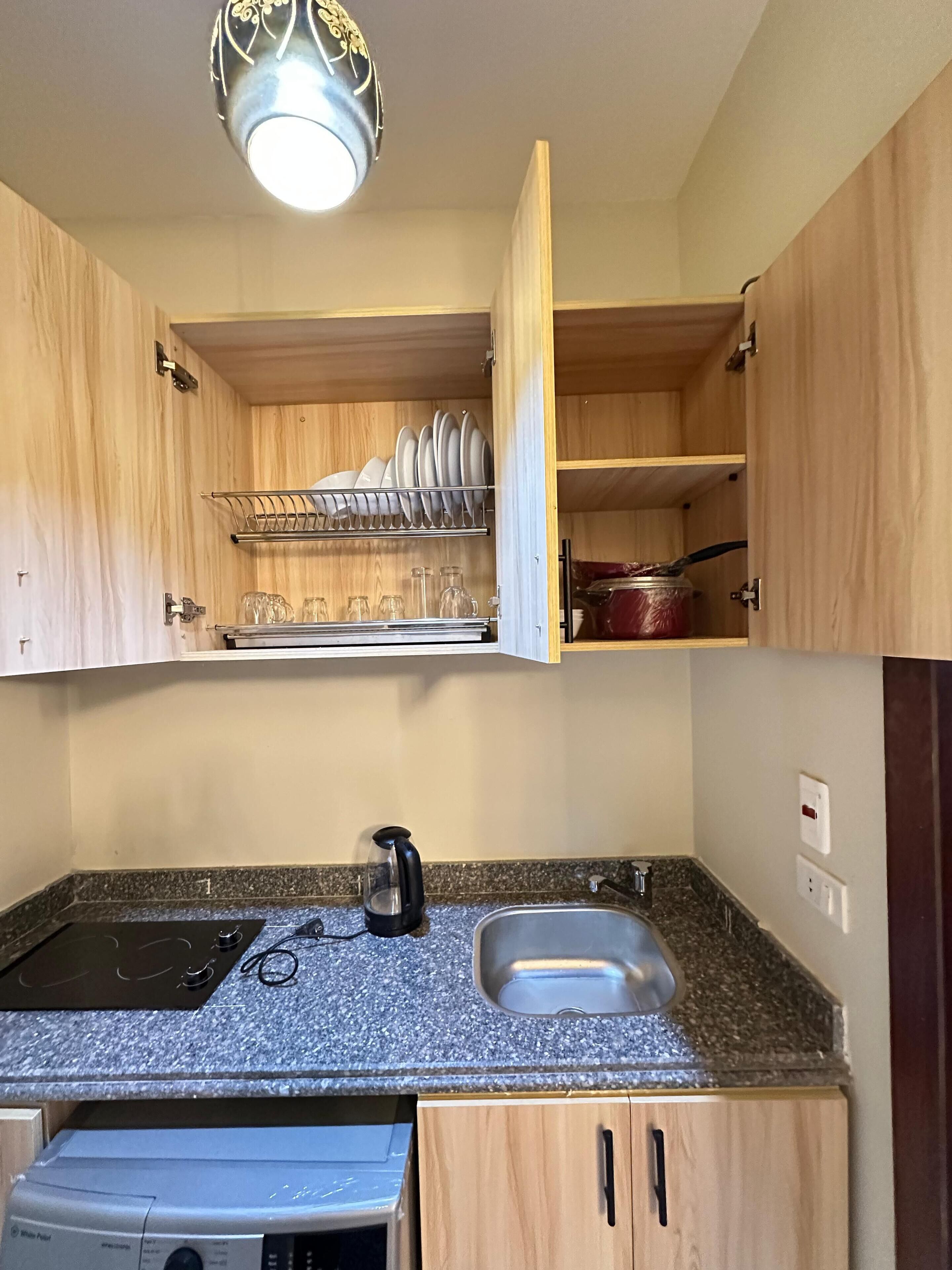 Uma cozinha compacta com armários de madeira, bancada de granito, lava-louças embutida e uma pia pequena.