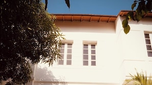 Edifício branco com entrada xadrez, cercado por vegetação exuberante e céu azul límpido.