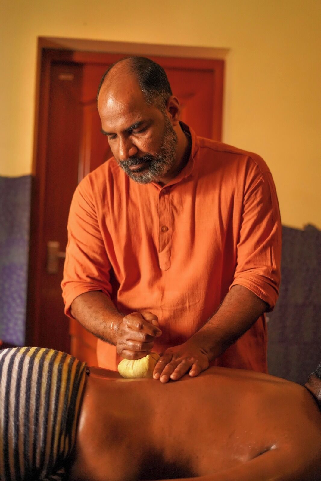 Uma pessoa vestindo uma camisa laranja realiza uma massagem em outra pessoa sentada em uma maca.