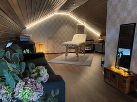 Quarto moderno e acolhedor com teto de madeira, cadeira de massagem, sofá, mesinha com luzes decorativas e radiador.
