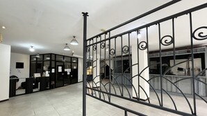 Um hall amplo com guarda-corpo de metal, piso ladrilhado e iluminação no teto.