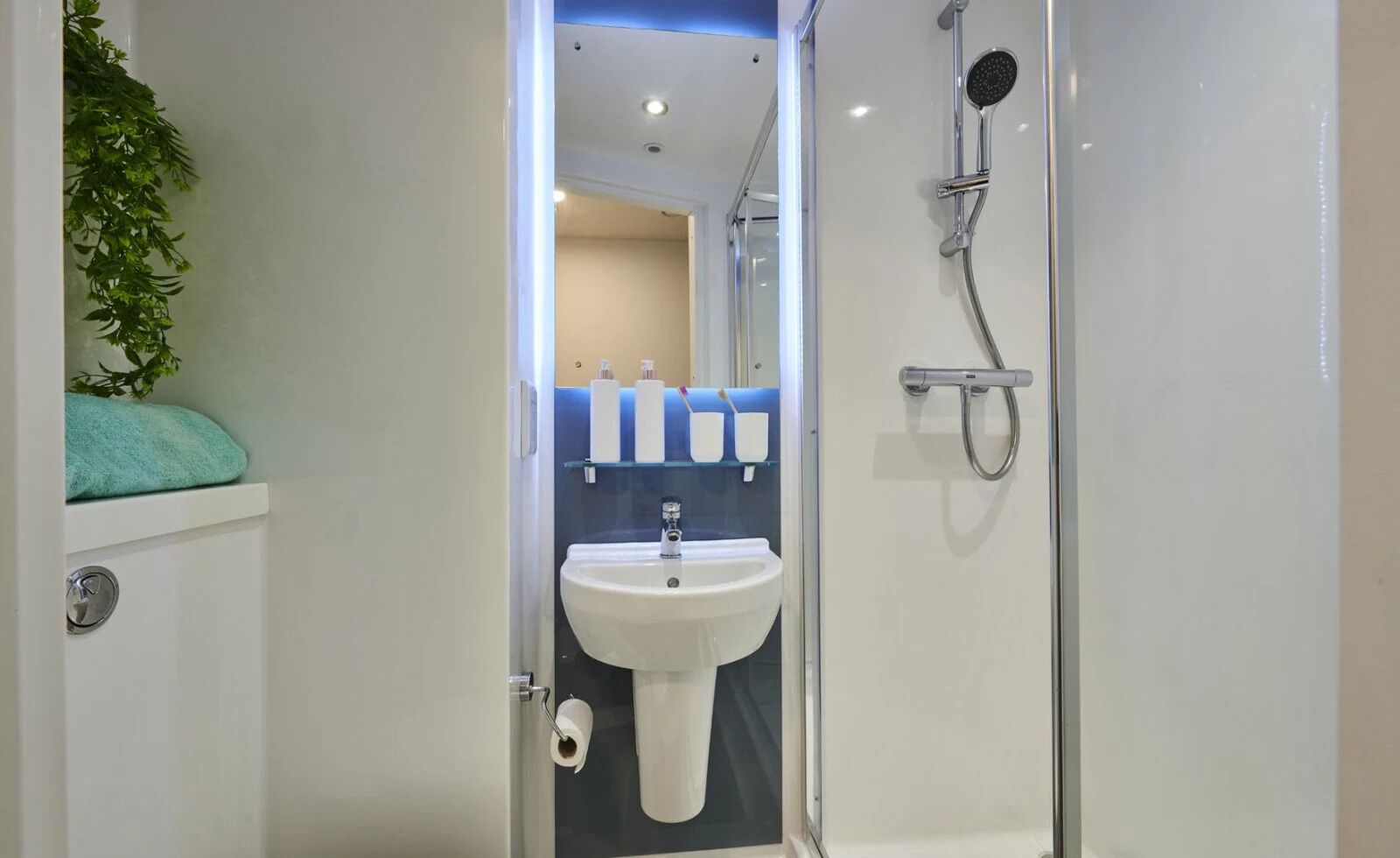 Um banheiro moderno com chuveiro em cabine de vidro, pia branca e parede azul.