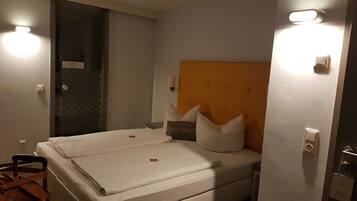 Quarto de hotel com cama, cabeceira, mesa de cabeceira e luminária fixada na parede.
