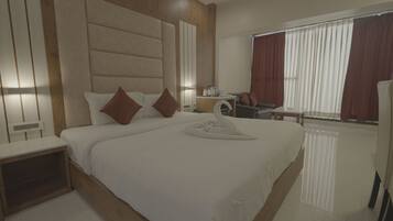 Quarto de hotel moderno com uma cama grande, cabeceira de madeira, mesa de cabeceira, escrivaninha pequena e janela com cortinas.