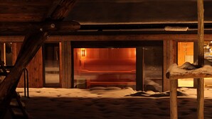 Uma cabana de madeira com interior acolhedor, uma cama visível e uma porta de vidro que dá para o exterior.