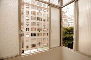 Vista pela janela de um edifício com vários andares, varandas e aparelhos de ar condicionado.