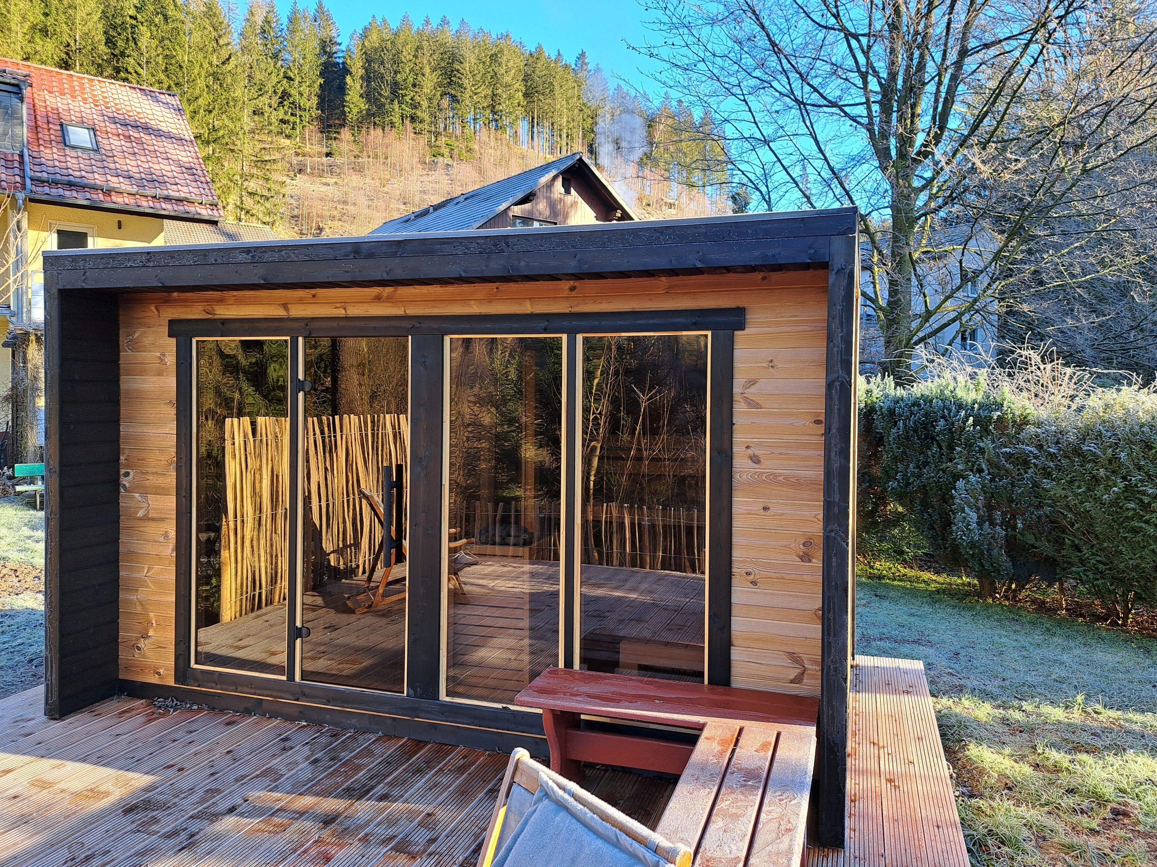 Uma cabana de madeira moderna com amplas janelas de vidro, um deck e vista para uma área arborizada.