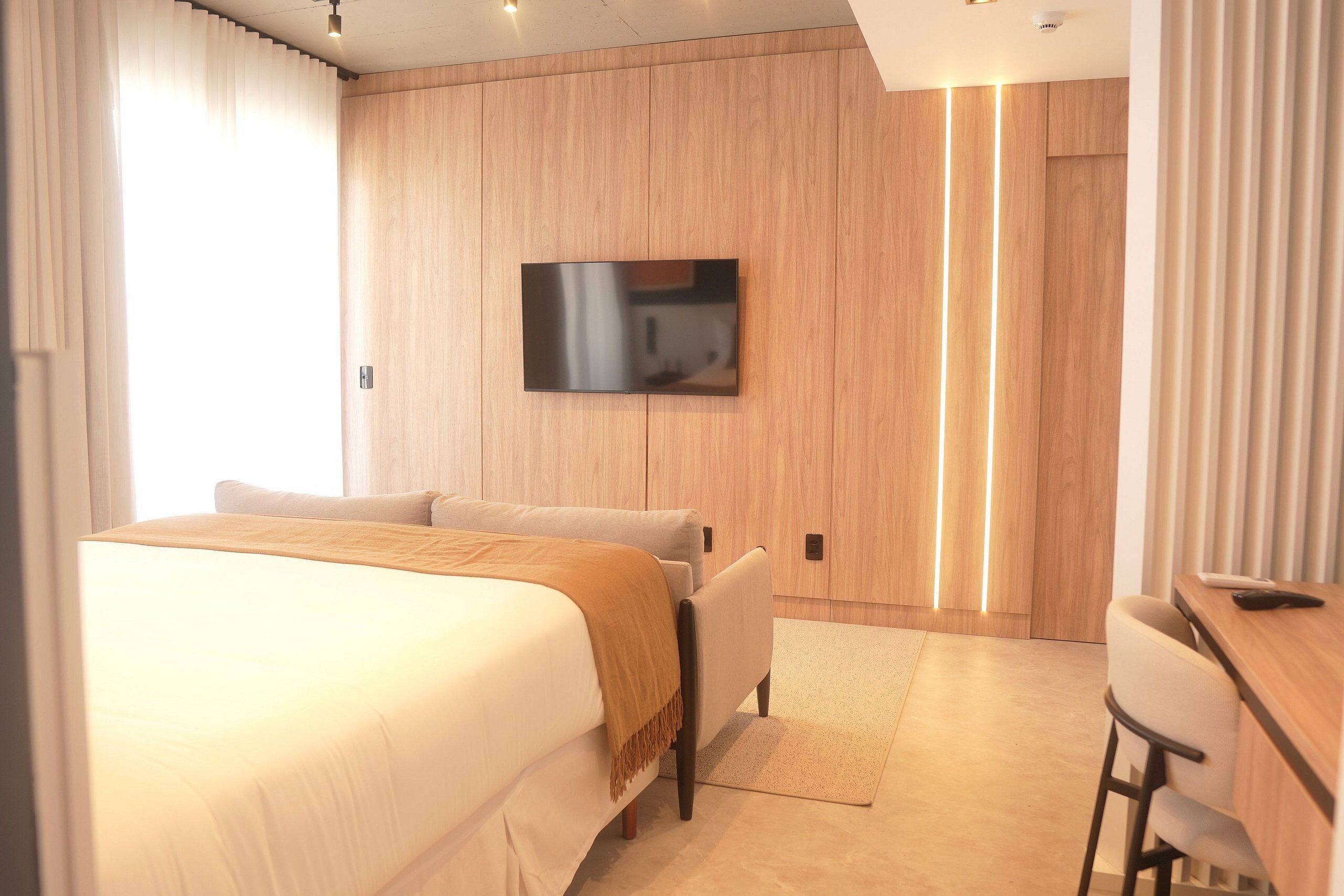 Quarto de hotel moderno com uma cama grande, uma escrivaninha e uma TV na parede.