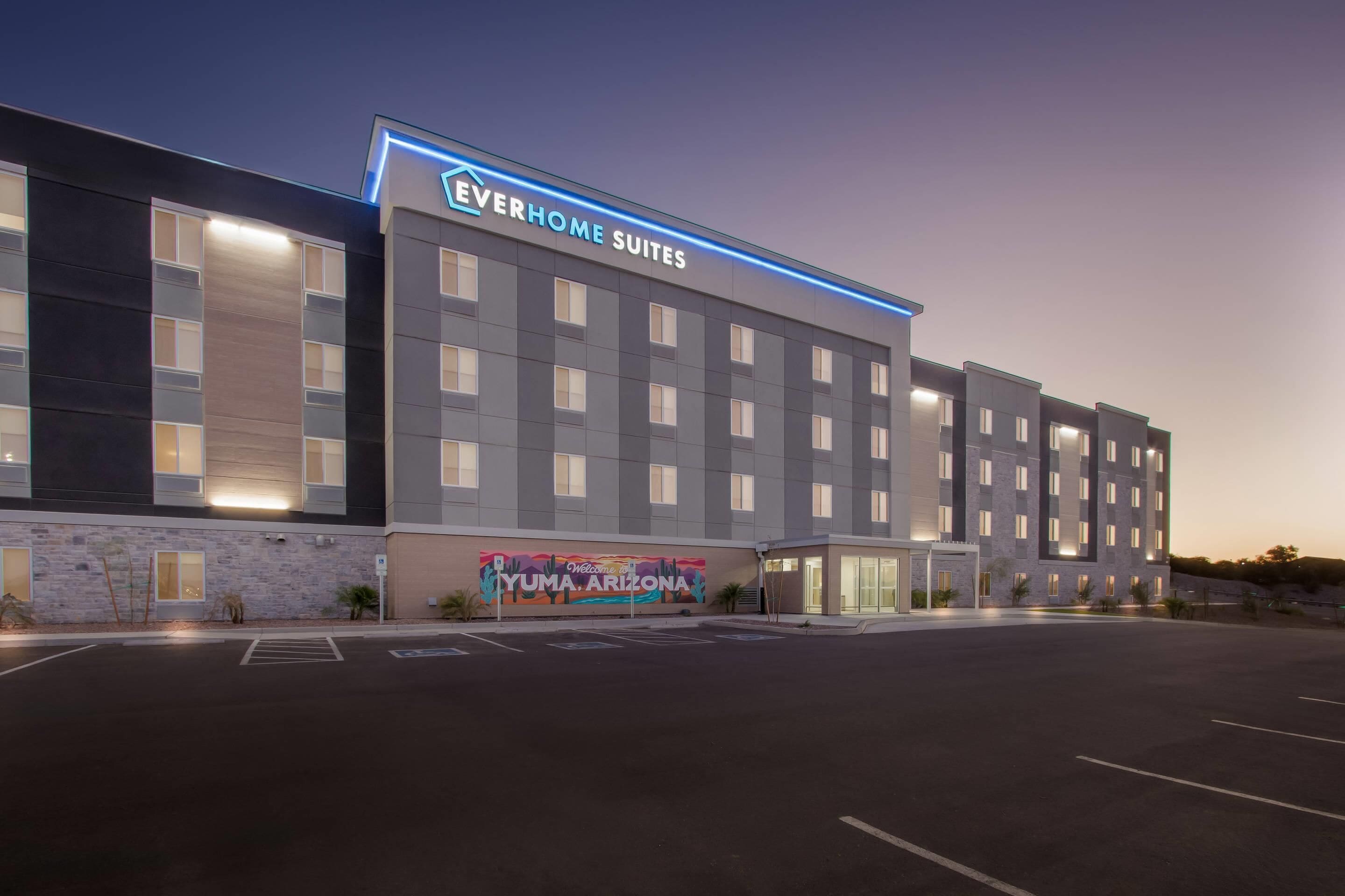Um hotel moderno com uma placa que diz "EVERHOME SUITES" e um mural dando as boas-vindas aos visitantes em Yuma, Arizona.