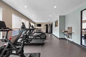Uma academia com equipamentos de ginástica, incluindo esteiras e bicicletas ergométricas, e uma televisão presa à parede.