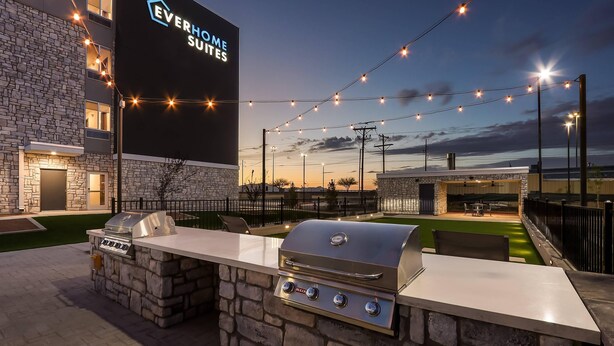 Uma área de cozinha externa com churrasqueira e grelha de pedra, luzes de fada e uma placa para EverHome Suites.