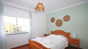 Quarto com cama de madeira, mesa de cabeceira, luminária na parede e janela com cortinas.