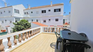 Um terraço com piso de azulejos, uma mesa com cadeiras e um corrimão com balaústres.