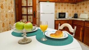 Uma mesa posta para o café da manhã, com uma tigela de maçãs, um copo de suco de laranja e um croissant sobre um guardanapo.