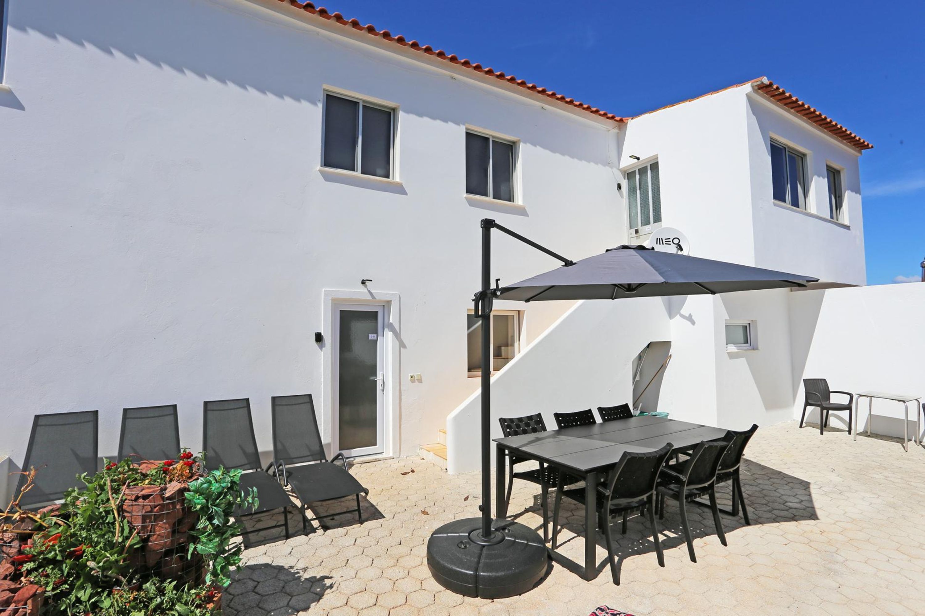 Uma área de pátio com mesa e cadeiras, um guarda-sol e um canteiro de tijolos com plantas.