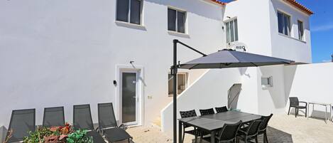 Uma área de pátio com mesa e cadeiras, um guarda-sol e um canteiro de tijolos com plantas.
