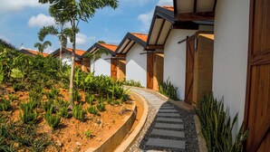 Uma passagem leva a uma fileira de edifícios brancos com telhados laranja, cercados por vegetação e uma borda de pedra.