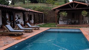 Piscina com espreguiçadeiras, varanda coberta e cerca de madeira.