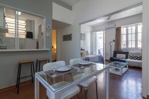 Uma sala de estar moderna com uma mesa de jantar de vidro, cadeiras brancas, um sofá e uma mesa de centro.