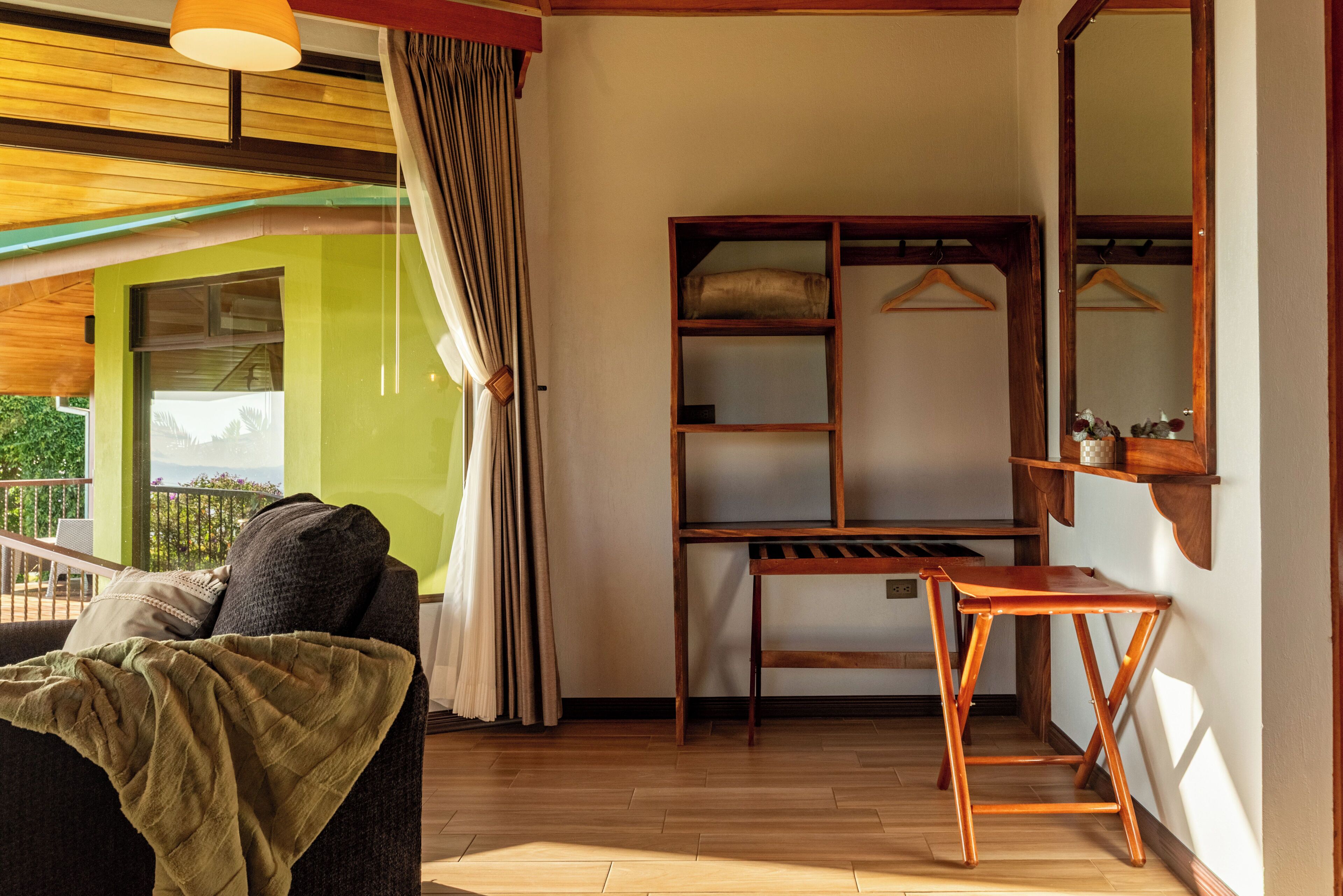 Quarto com sofá, mesa de madeira, espelho e janela com cortinas.