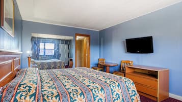 Quarto com uma cama grande, penteadeira de madeira, escrivaninha, cadeira, televisão fixada na parede e janela com cortinas.