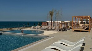 Uma área à beira da piscina com espreguiçadeiras, piscina e vista para o mar.