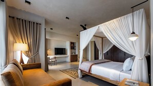Quarto de hotel com cama, sofá, escrivaninha, televisão e banheiro.