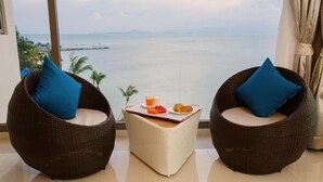 Duas cadeiras de vime com almofadas azuis, uma mesa pequena com itens de café da manhã e vista para o mar.