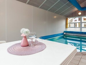 Uma área junto à piscina com uma mesa branca, um vaso rosa e um copo de água.